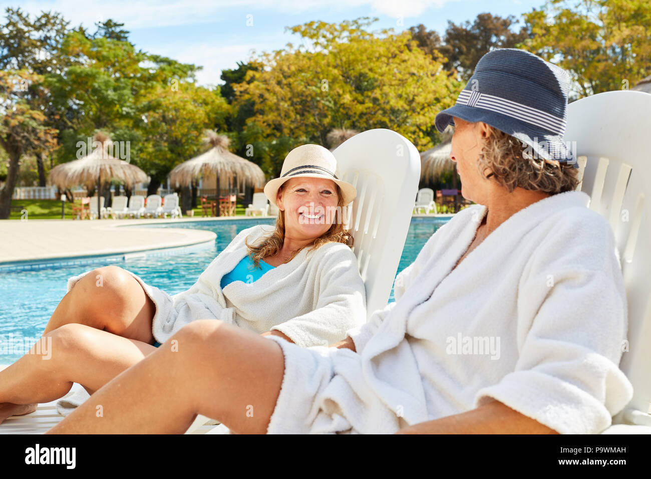 Two friends relax by the swimming pool at the Wellness Hotel Stock ...