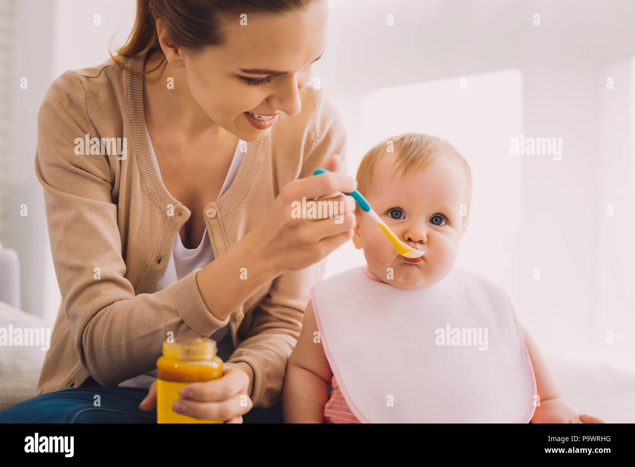 Healthy food. Cheerful reliable babysitter carefully feeding a serious ...