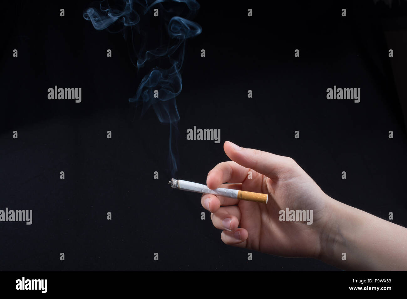 Hand is holding smoking cigarette with smoke around Stock Photo - Alamy