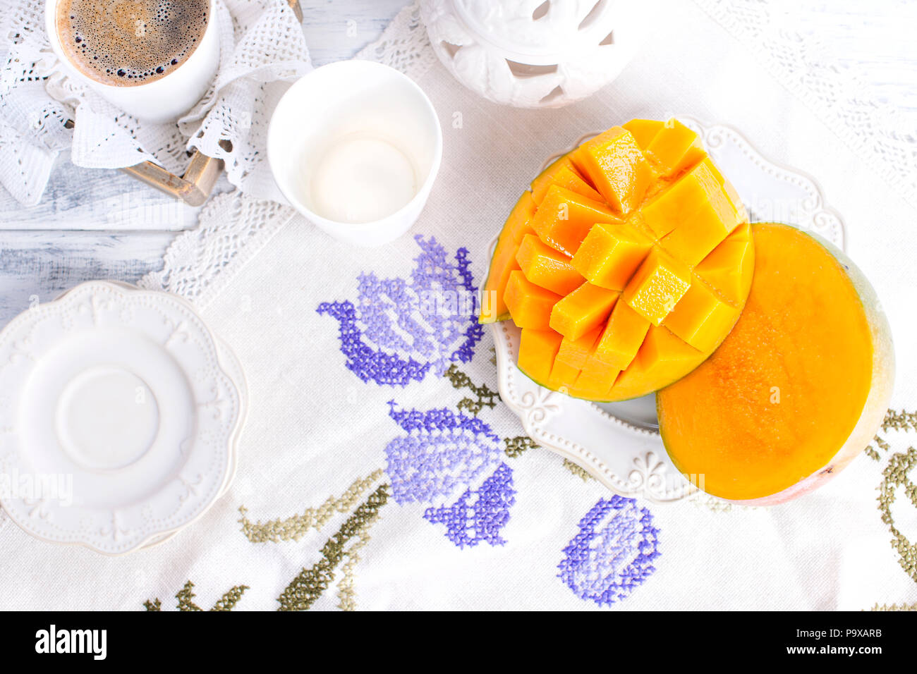 The sweet mango fruit is cut into cubes. On a lace tablecloth and a cup ...