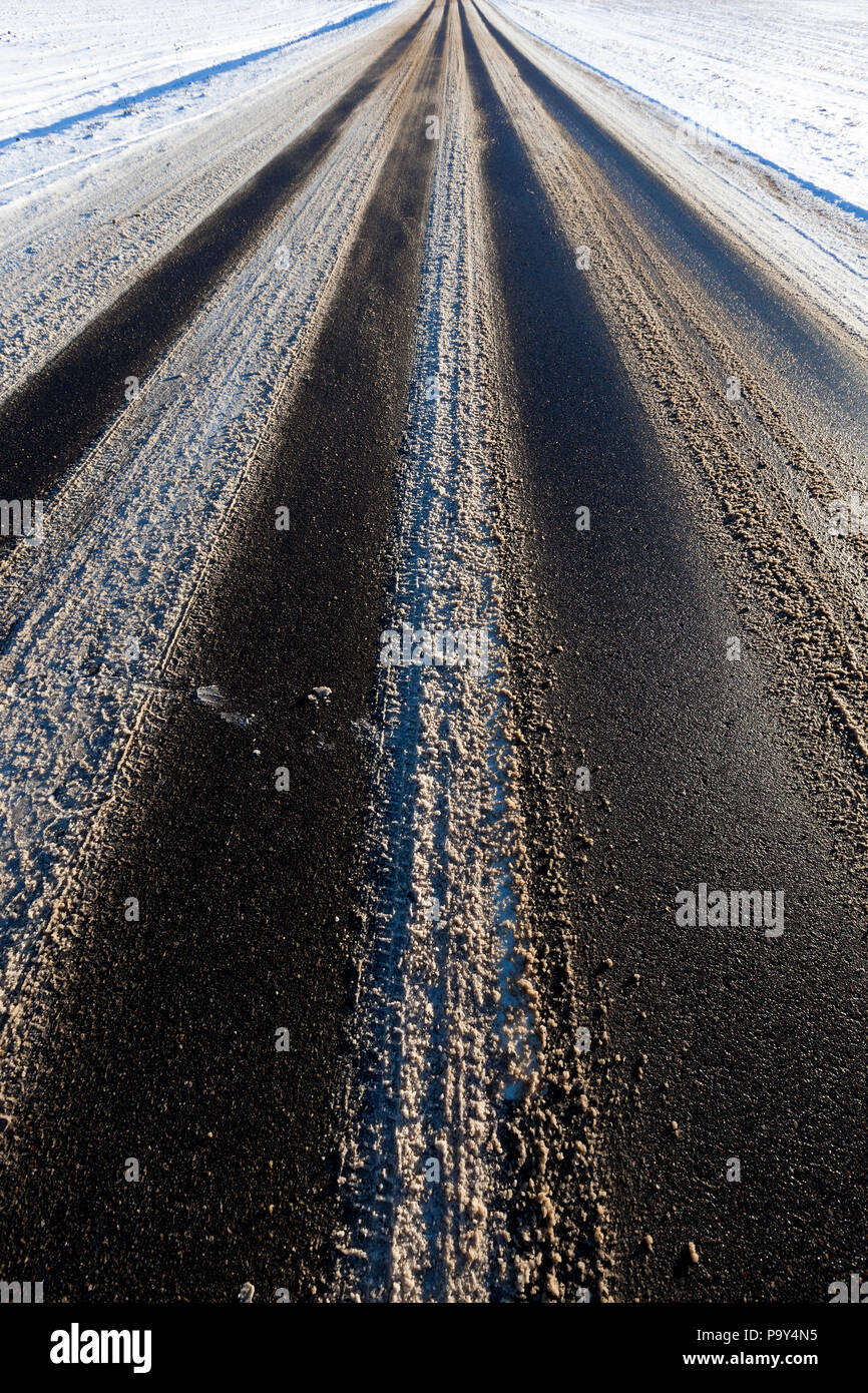 asphalt road on which the snow melted after the passed cars and ruts ...