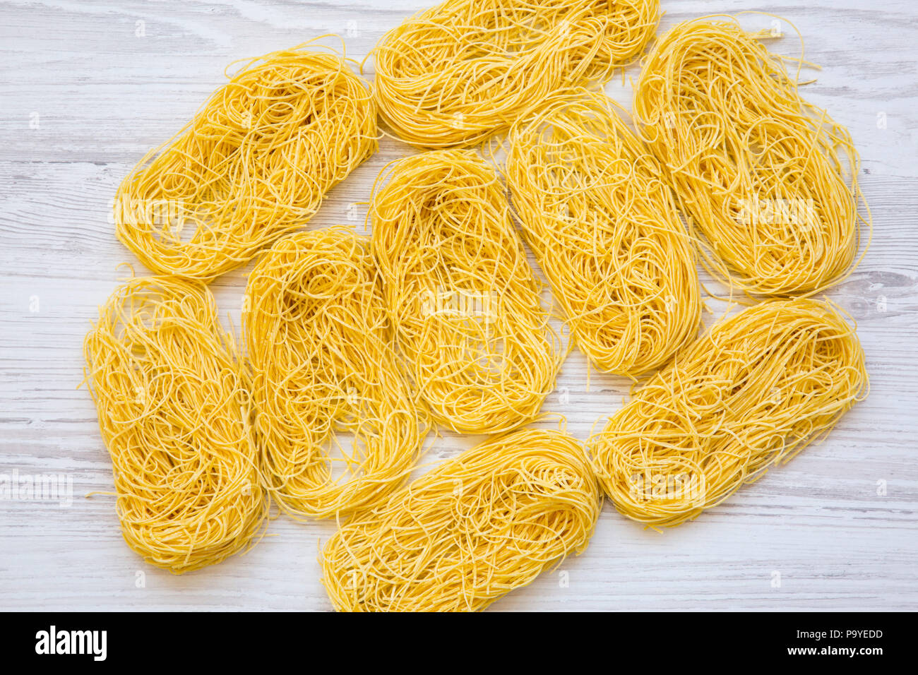 Uncooked pasta tagliolini on white wooden backgroundm top view. Flat ...