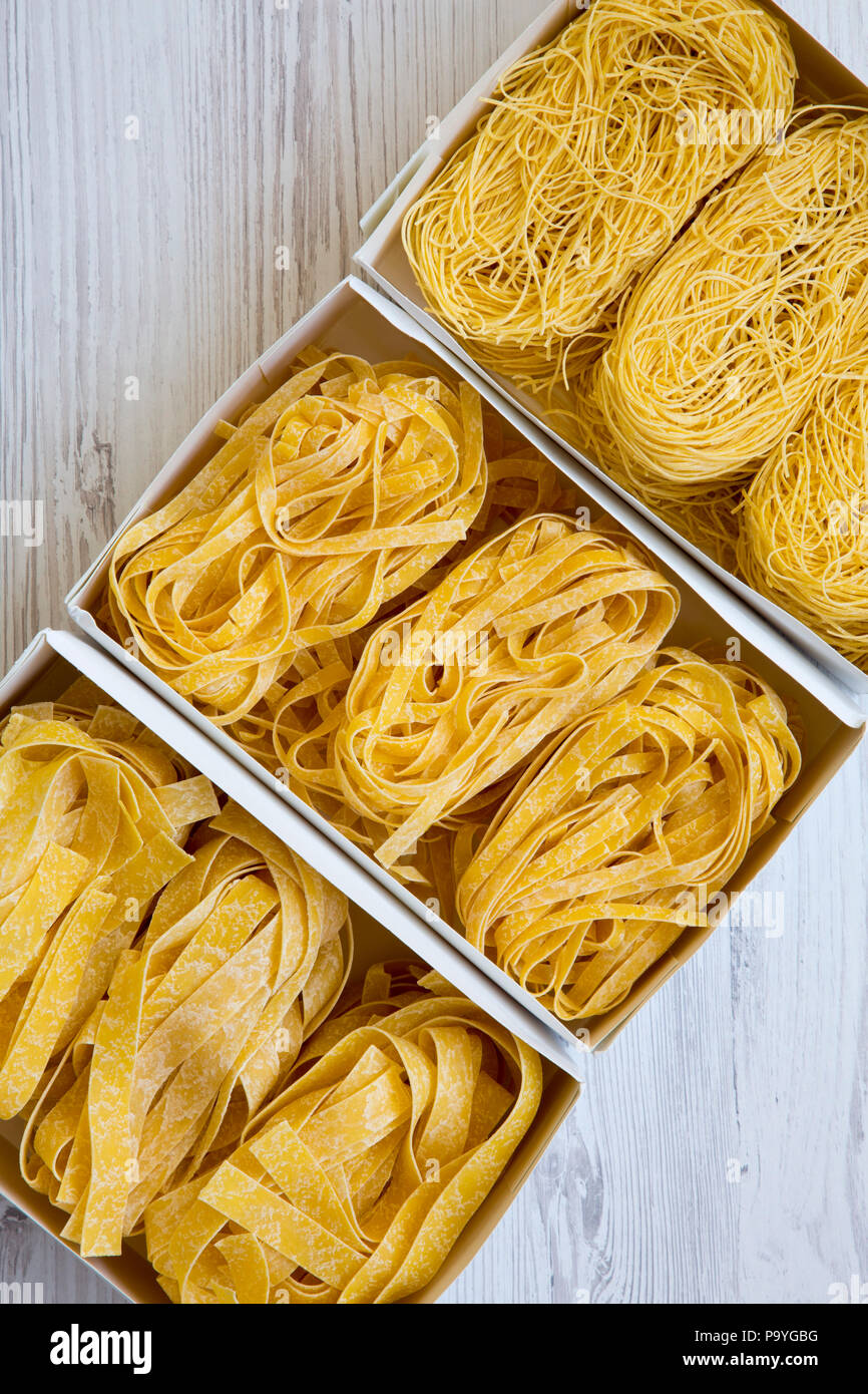 Set of different uncooked pasta in paper boxes on a white wooden table ...