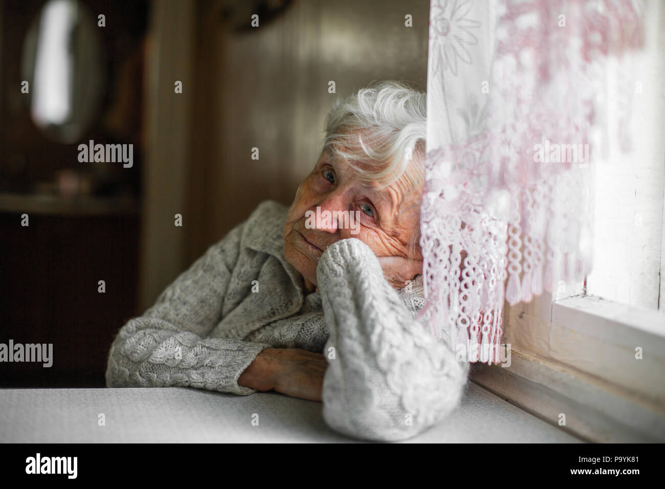 Sad old woman sitting near the window Stock Photo - Alamy