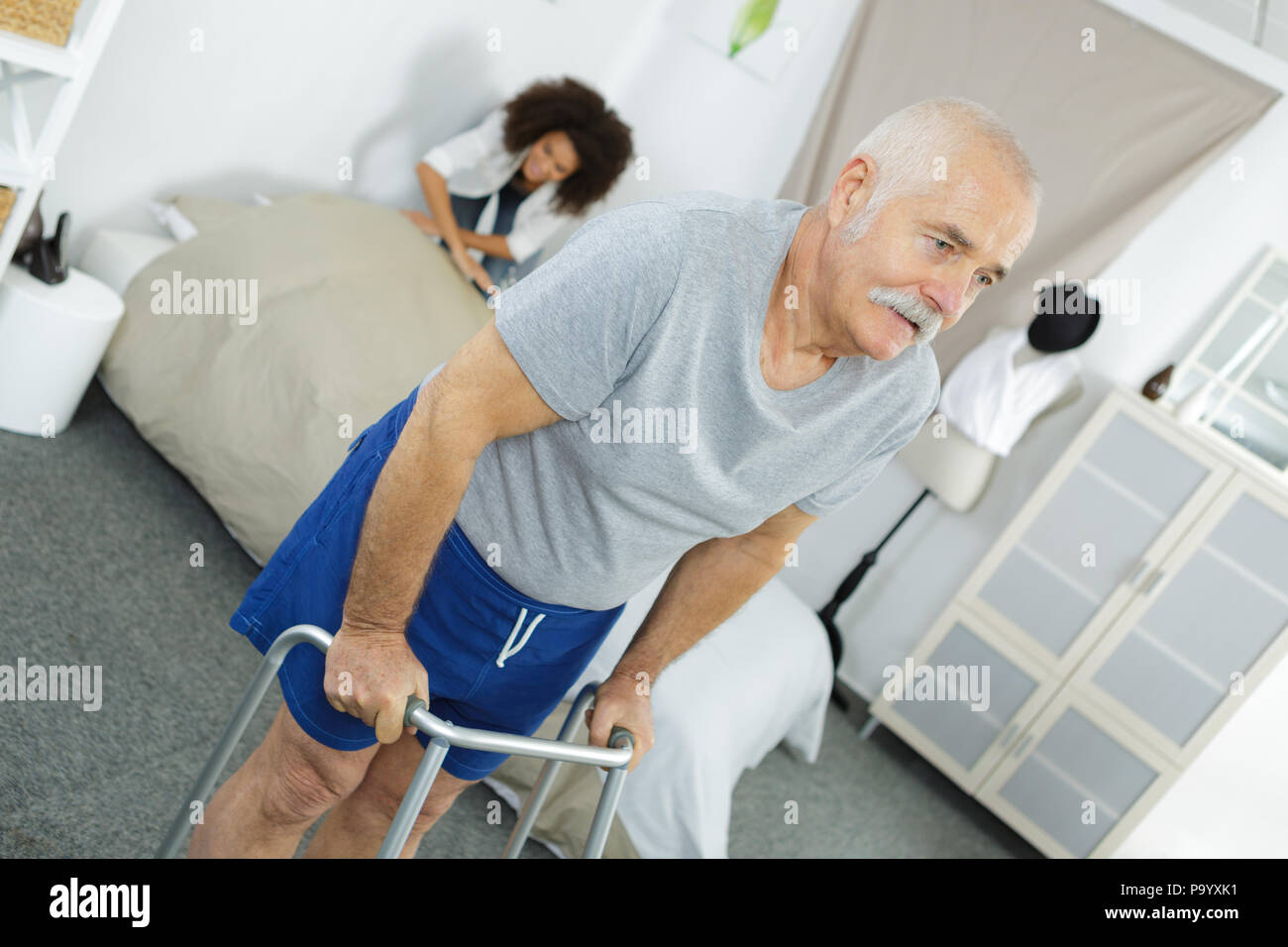 nurse assisting an elderly man with a walking frame Stock Photo - Alamy
