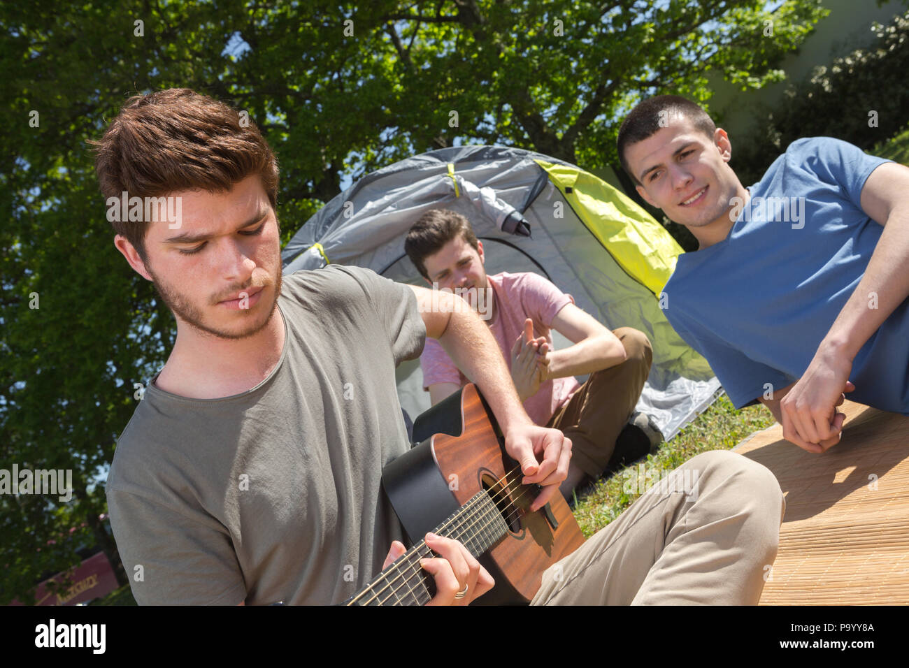 friends sitting near bonfire smiling embracing resting playing guitar ...