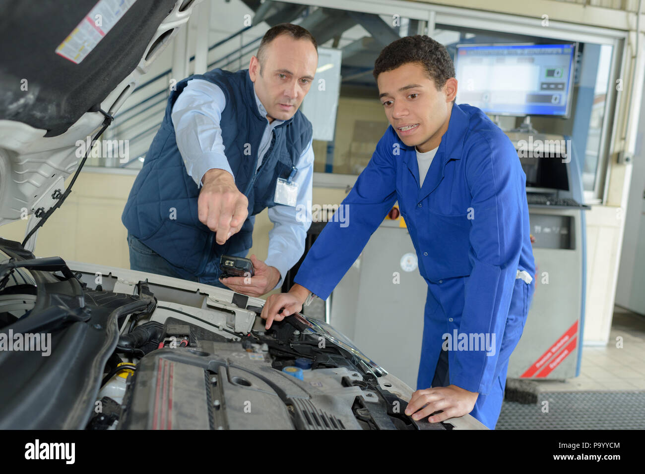mechanic giving instructions to trainee looking at car engine Stock ...