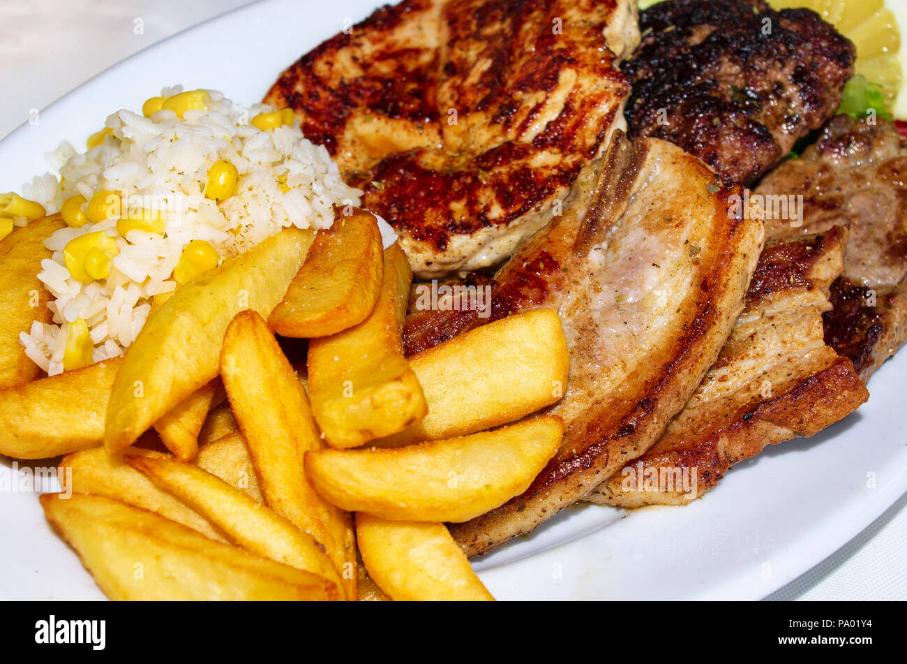 Grilled pork and goat meat dish with French fries and rice with corn ...