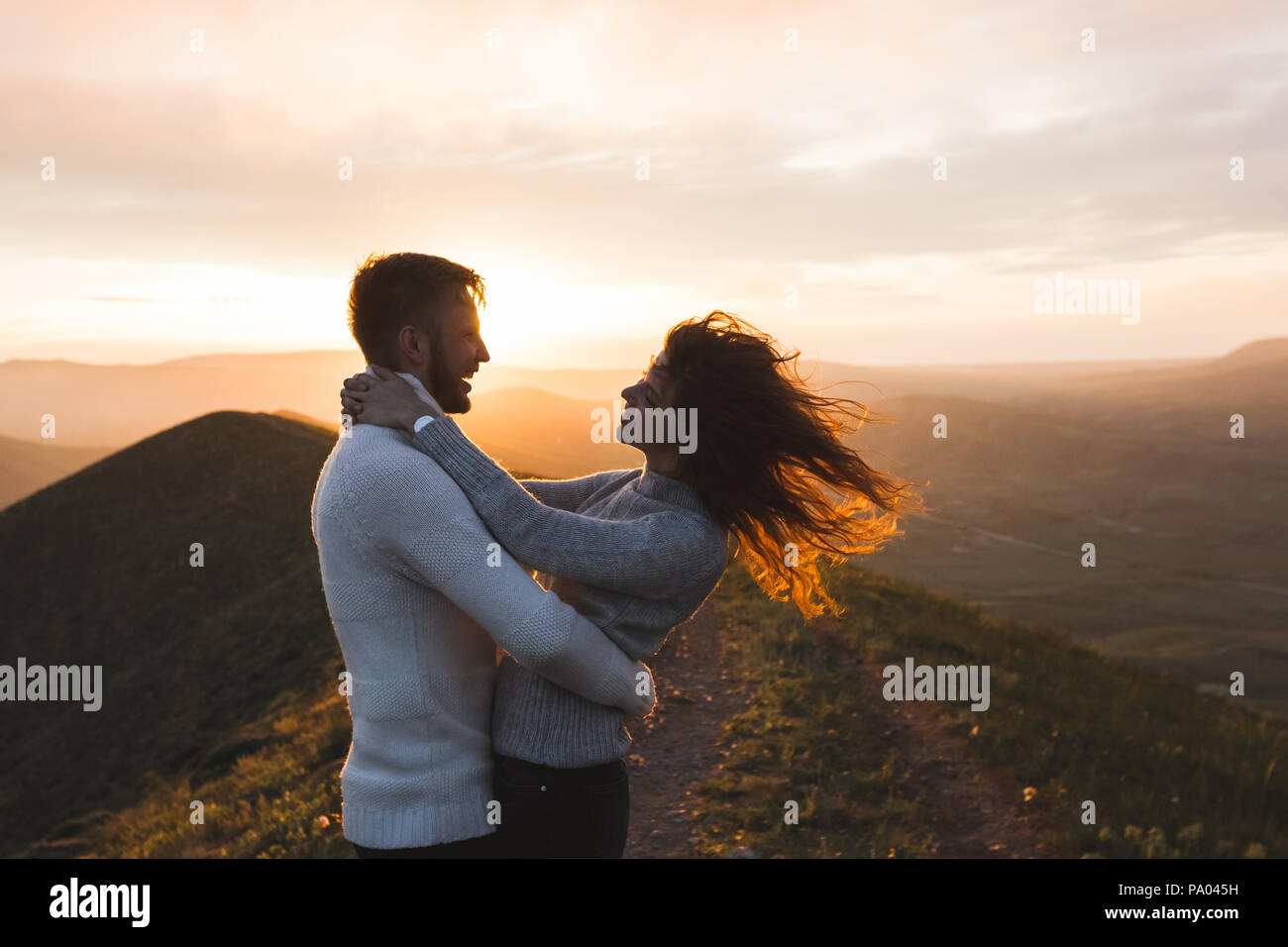 Happy couple hugging and kissing at sunset witn amazing mountain view ...