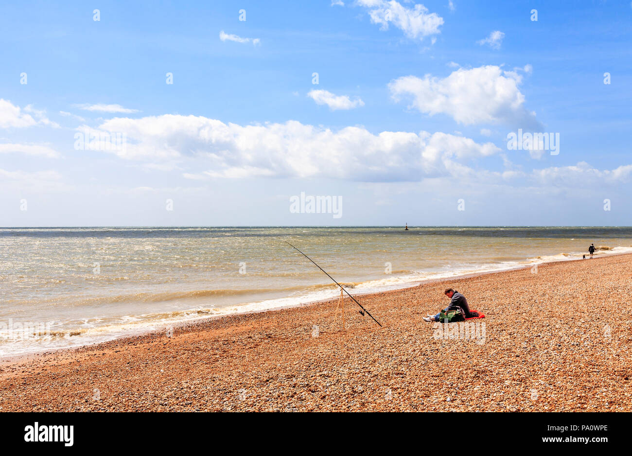 Lone sea fisherman fishing from the seashore on the shingle beach at ...