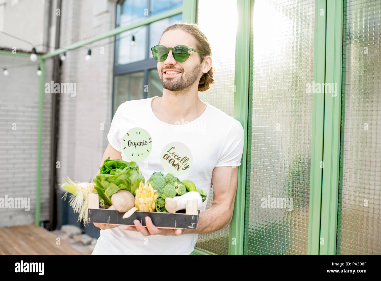 Portrait of a handsome vegetarian man standing with box full of organic ...