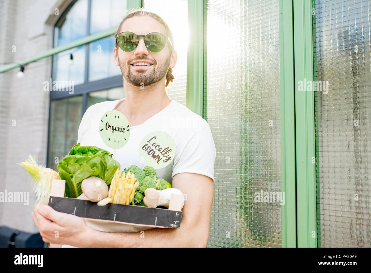 Portrait of a handsome vegetarian man standing with box full of organic ...