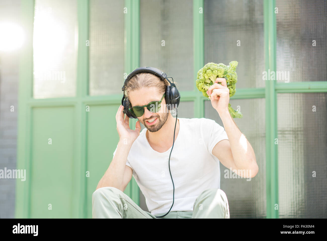 Funny portrait of a man listening to the music shaking with broccoli ...
