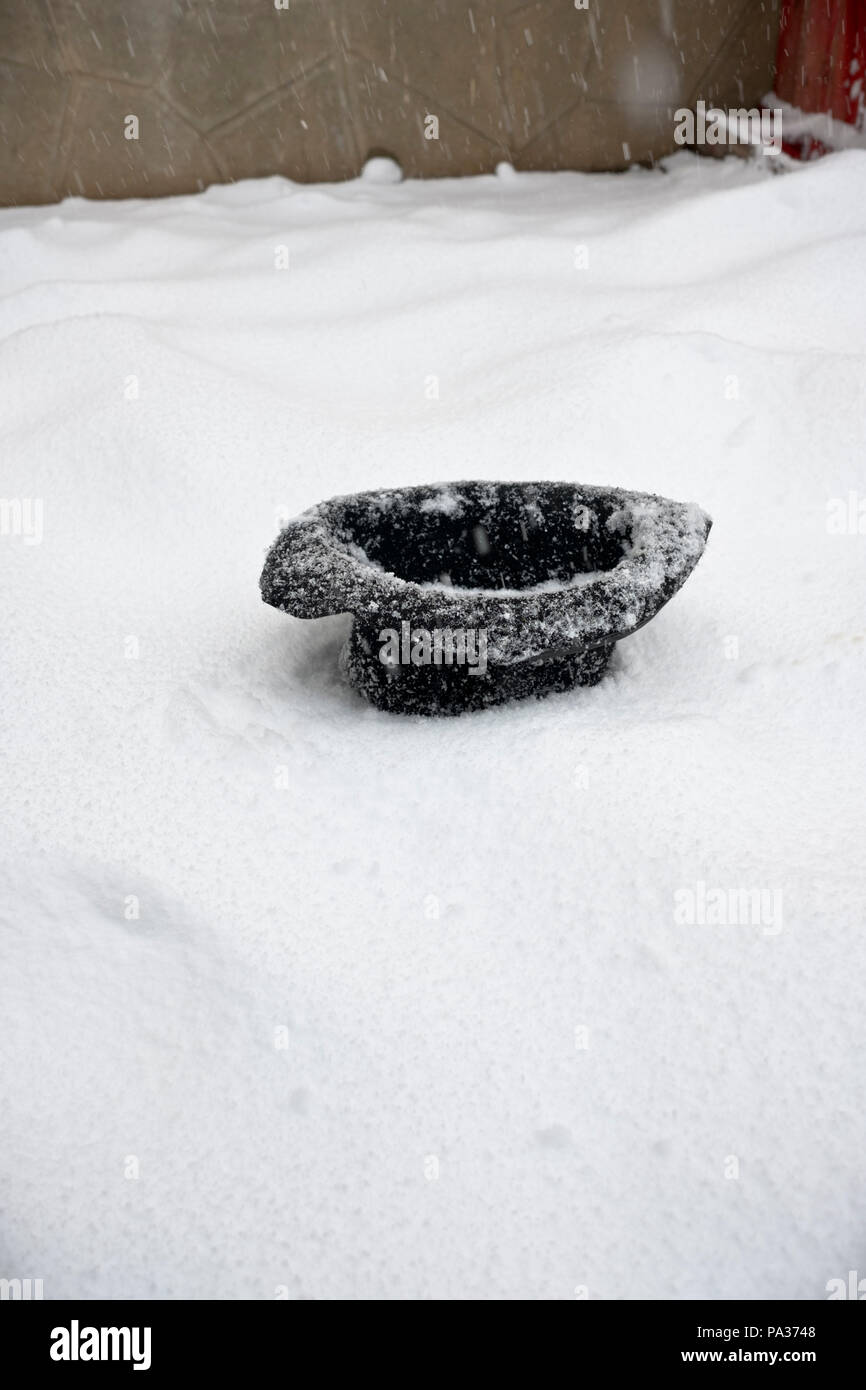 an old battered black felt top hat lies in the snow slowly being ...