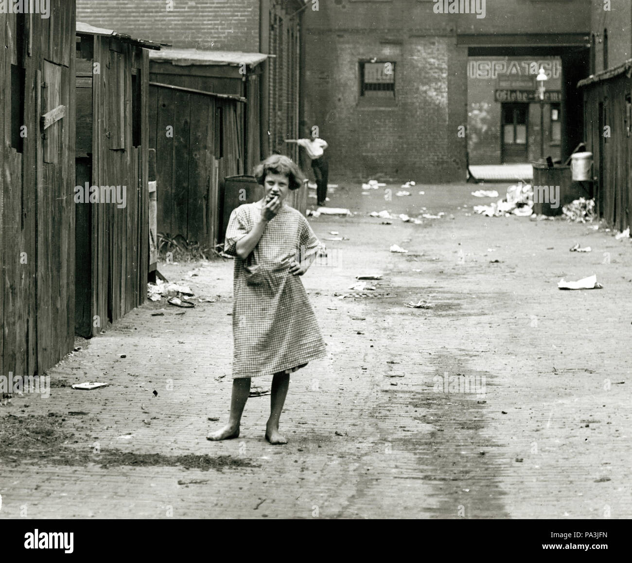 . English: Title: Barefoot girl eating an apple in a trash-filled alley ...