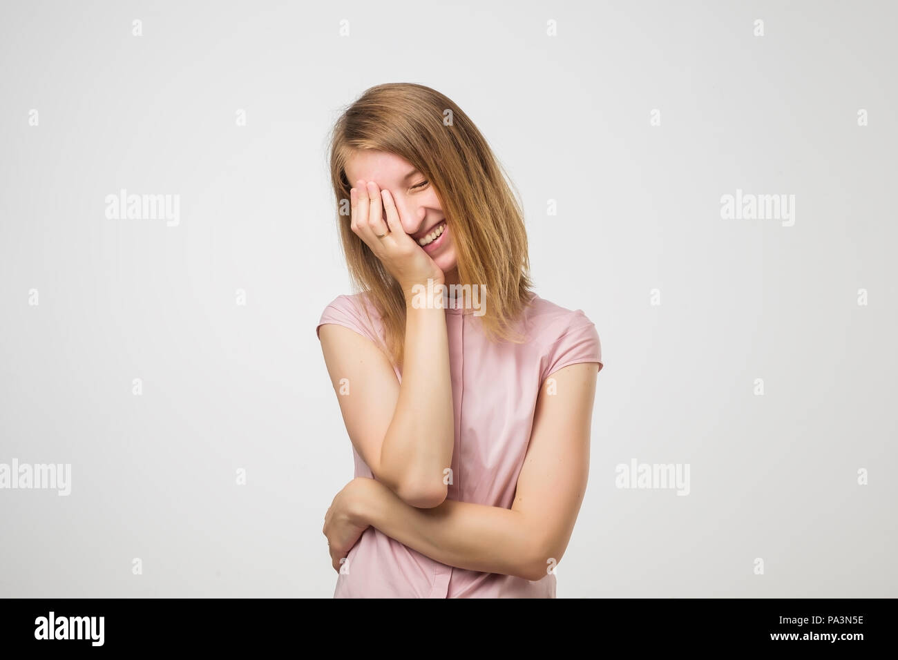 Studio shot of good looking young female giggles joyfully, covers mouth ...