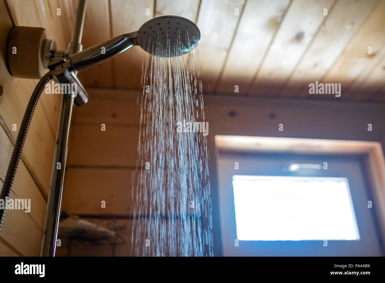 Shower head with flow of water closeup in wooden bathroom. Wasting of ...