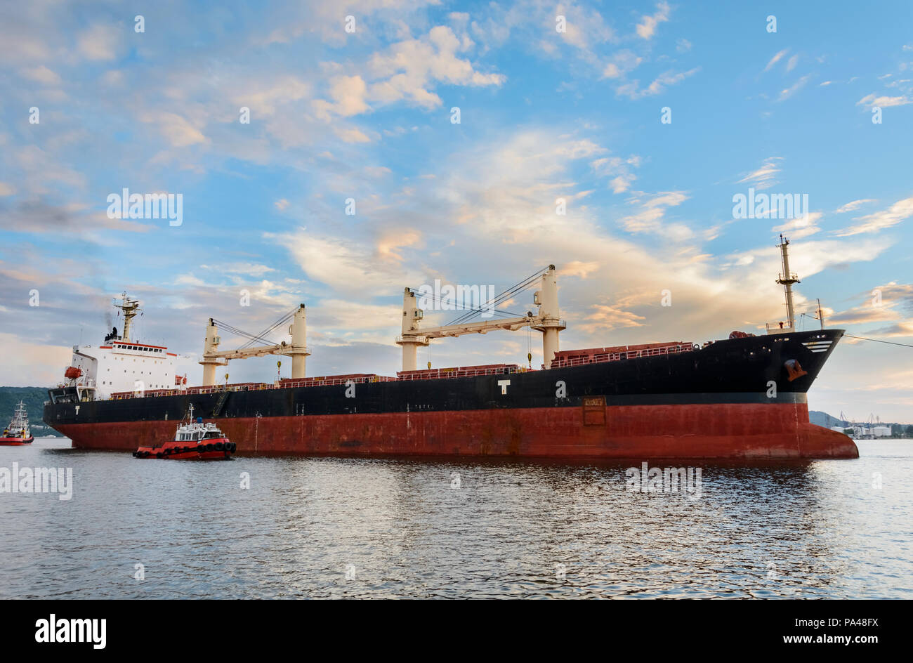 Tug boat entering the harbor with big cargo boat Stock Photo - Alamy