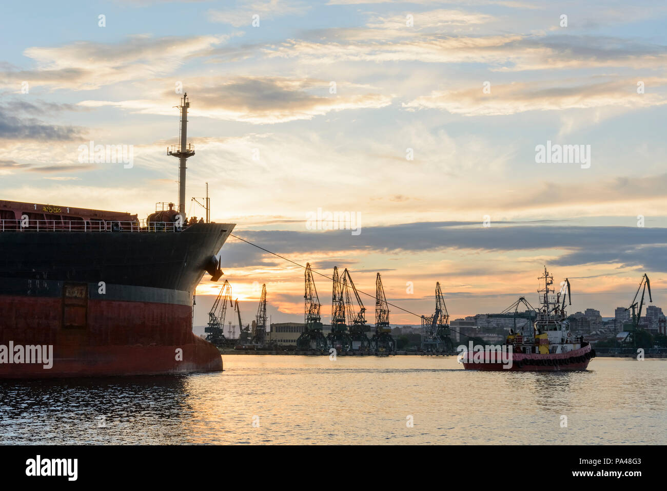 Tug boat entering the harbor with big cargo boat Stock Photo - Alamy