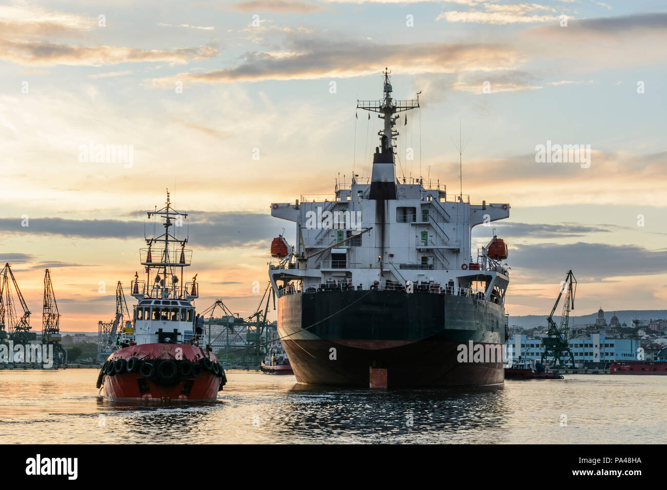 Tug boat entering the harbor with big cargo boat Stock Photo - Alamy