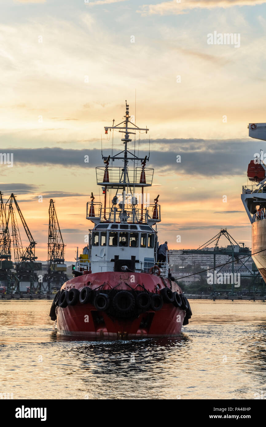 Tug boat entering the harbor with big cargo boat Stock Photo - Alamy