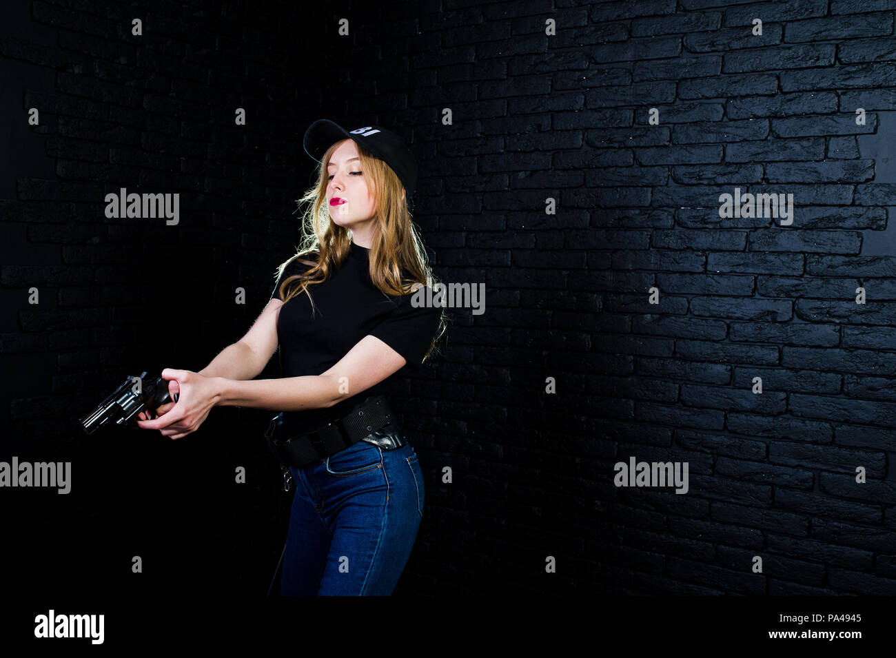 FBI female agent in cap and with gun at studio against dark brick wall ...