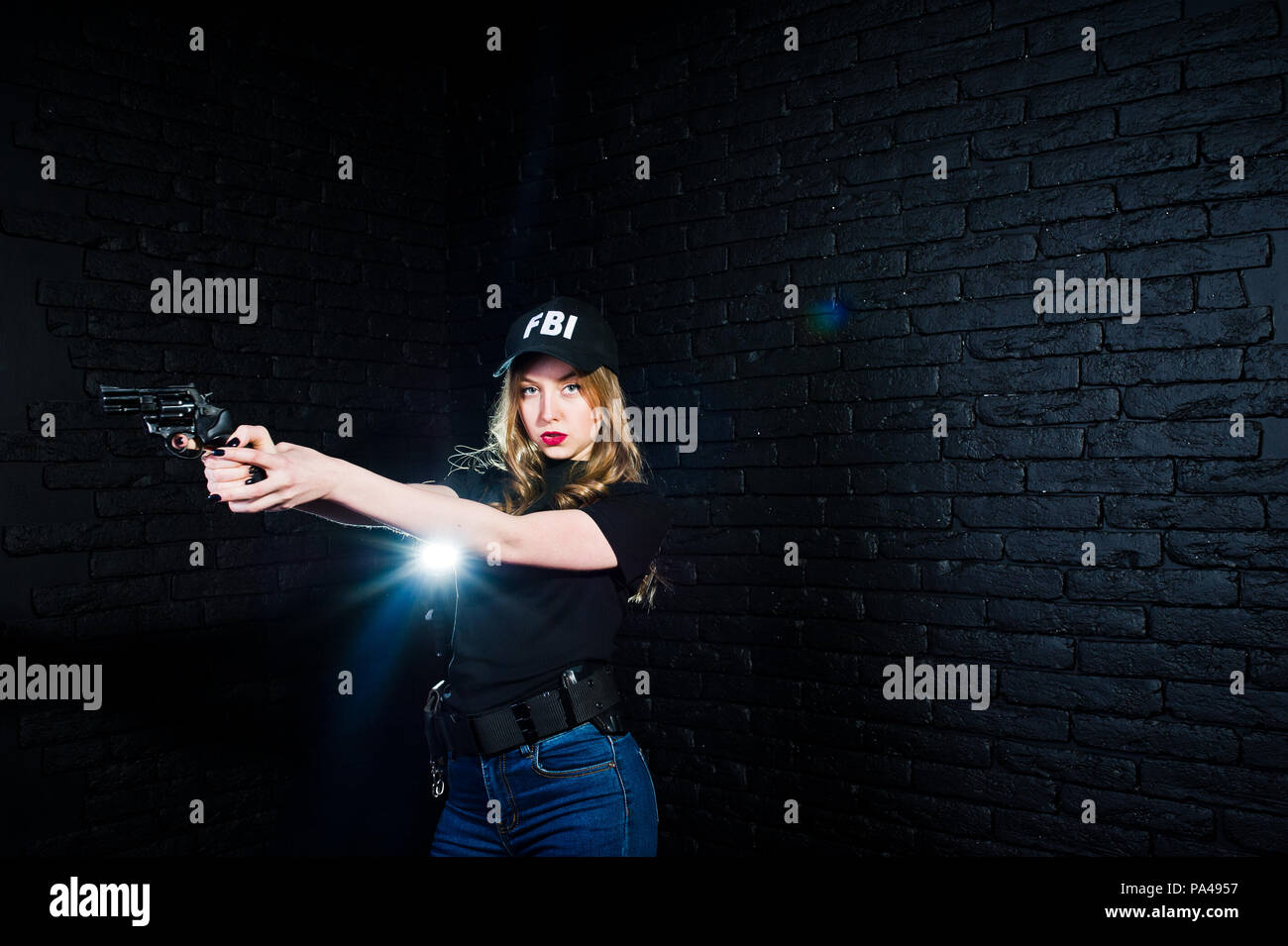 FBI female agent in cap and with gun at studio against dark brick wall ...