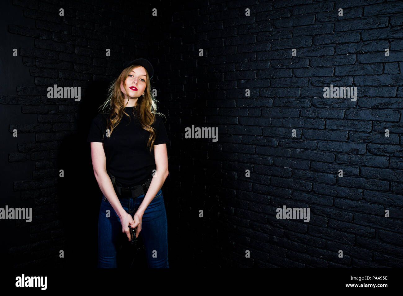 FBI female agent in cap and with gun at studio against dark brick wall ...