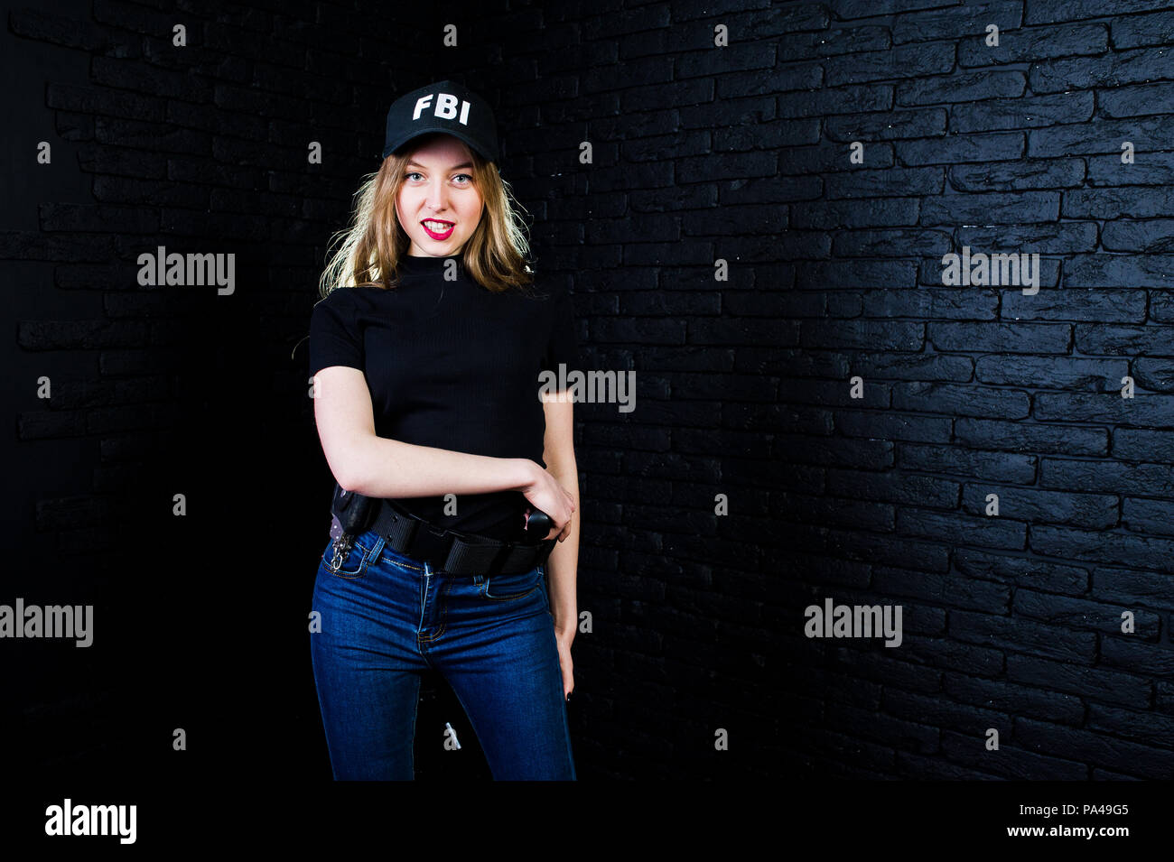 FBI female agent in cap and with gun at studio against dark brick wall ...