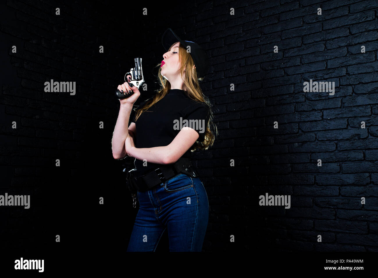 FBI female agent in cap and with gun at studio against dark brick wall ...