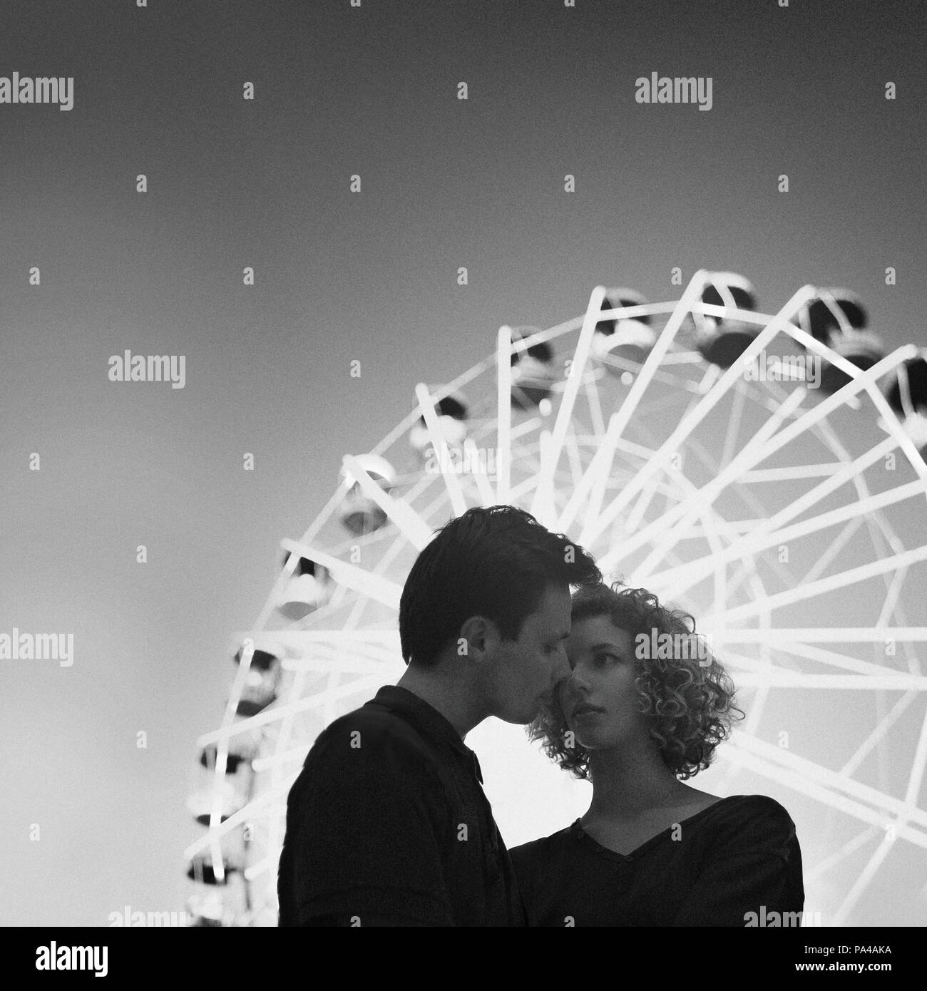 Romantic young couple in front of Ferris wheel in amusement park. Boy ...