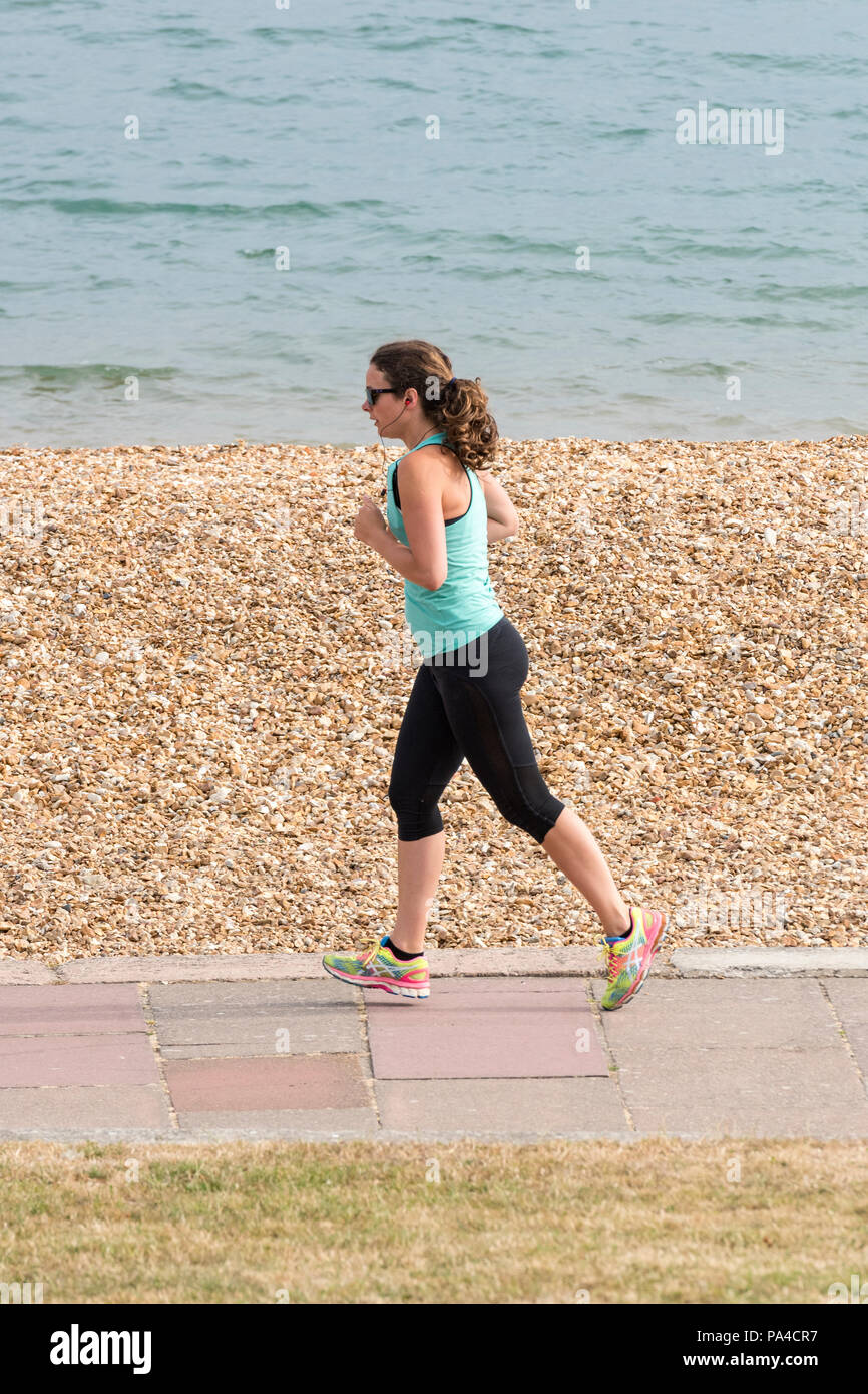 a young woman jogging along a beach on a seafront wearing sports gear ...