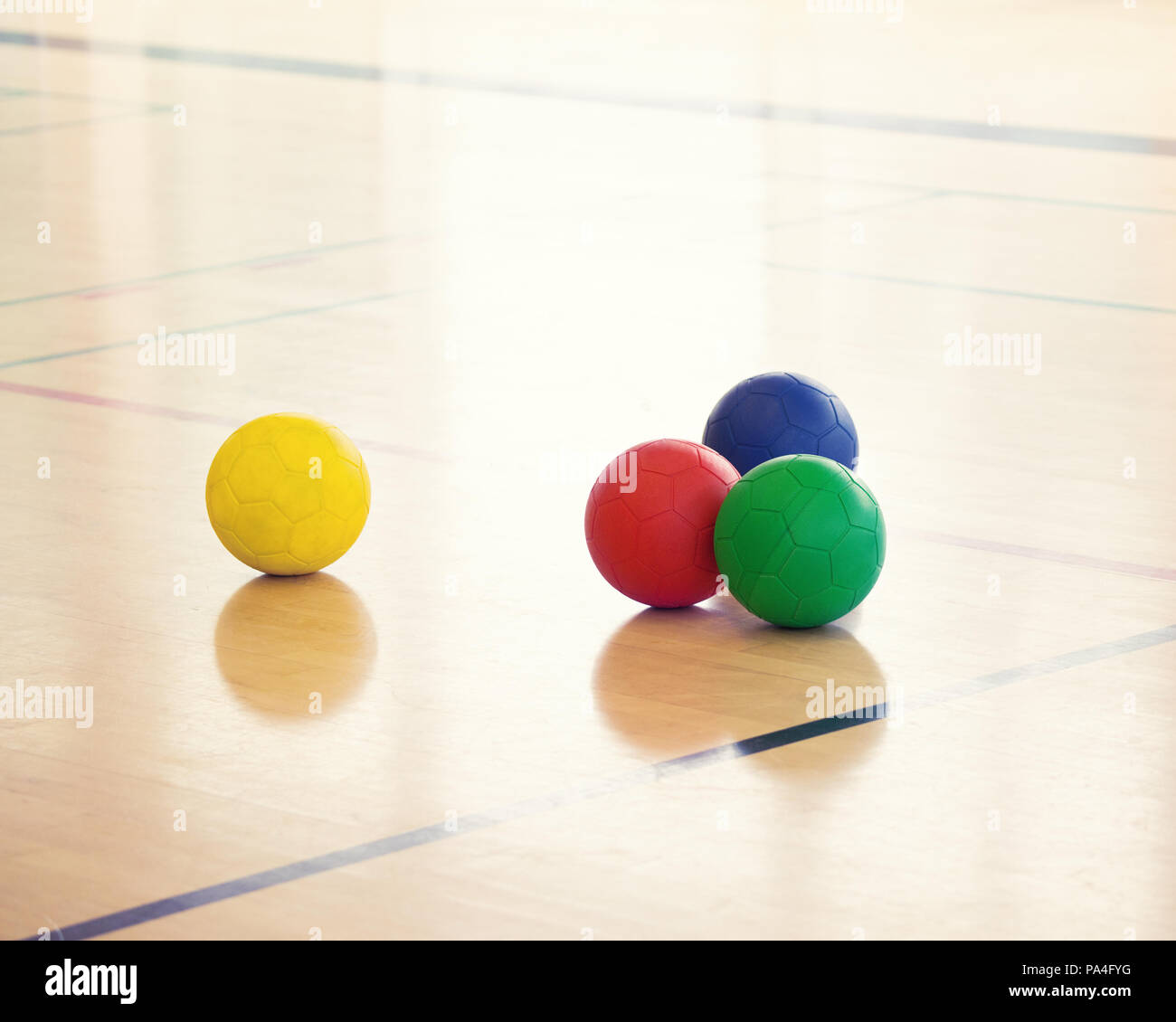 Set group of four colorful sports balls laying on the floor in gym, one ...
