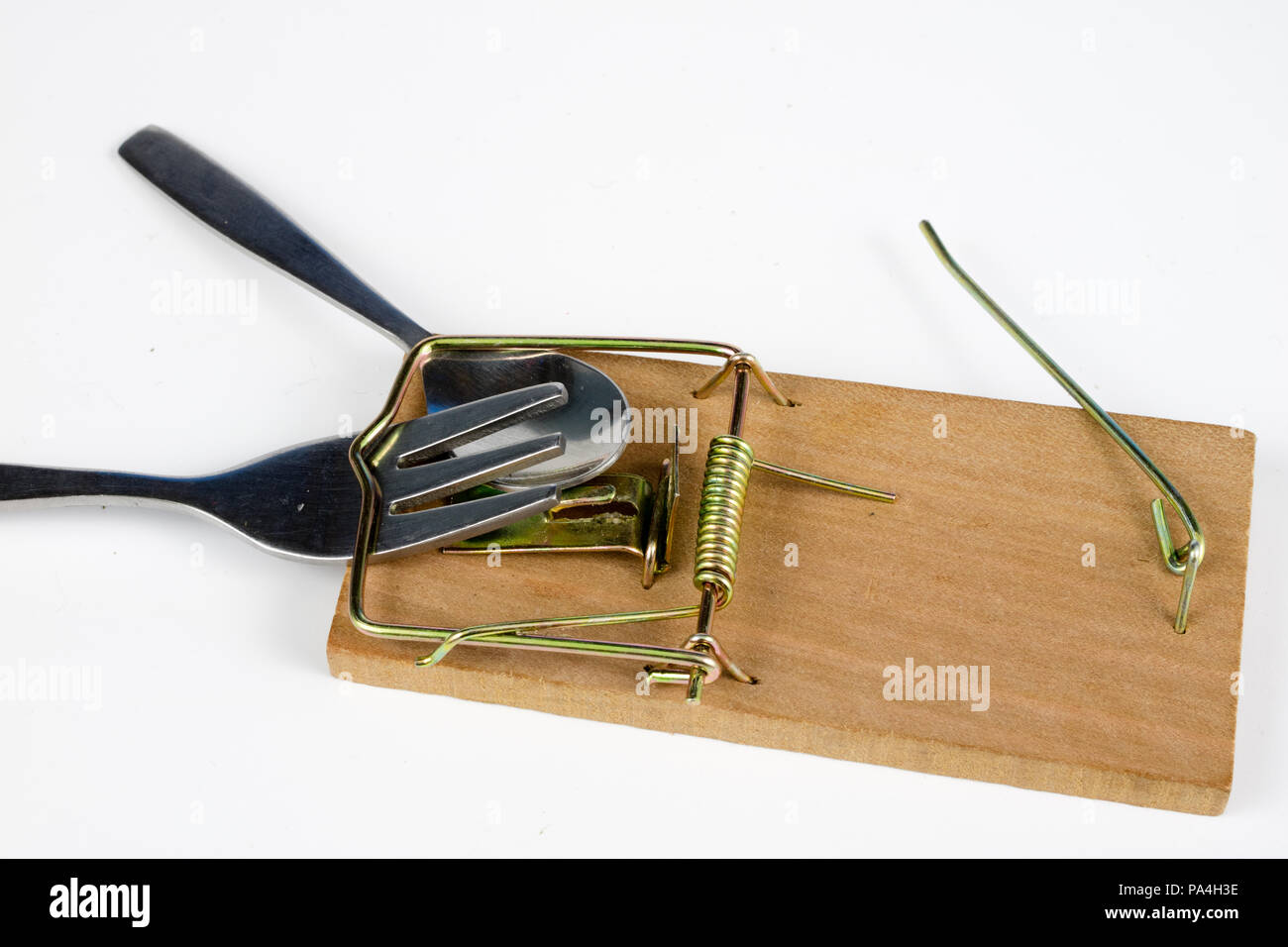 Cutlery and mousetrap on a white table. Fork and spoon caught in a trap ...