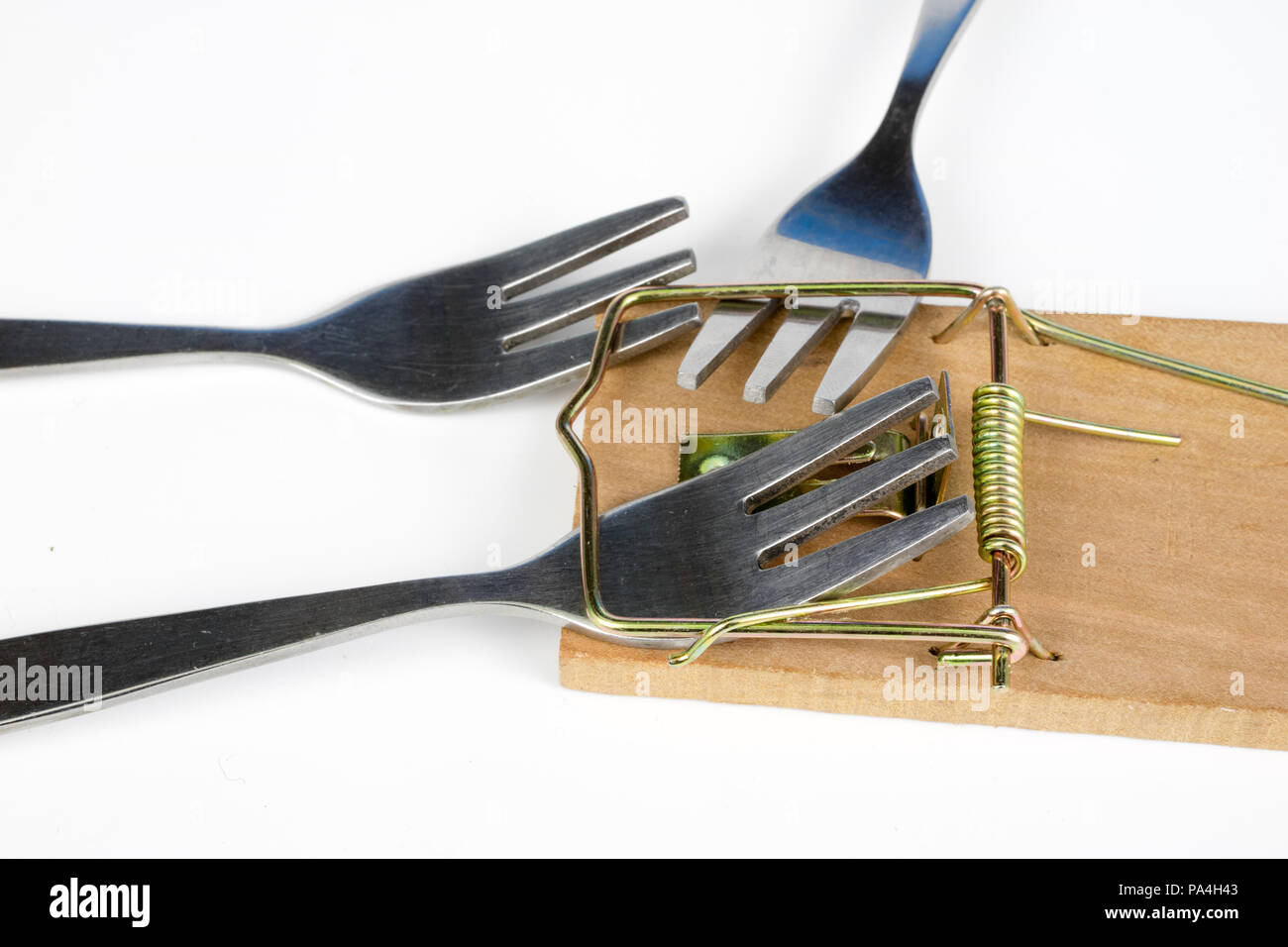 Cutlery and mousetrap on a white table. Fork and spoon caught in a trap ...