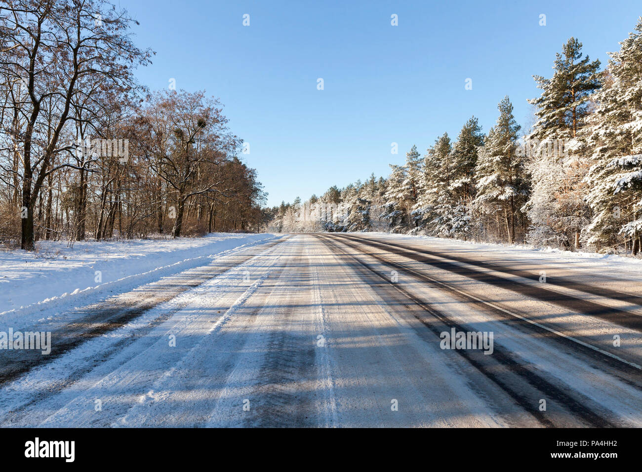 wide straight asphalt road in the winter season and Ruts from cars on ...