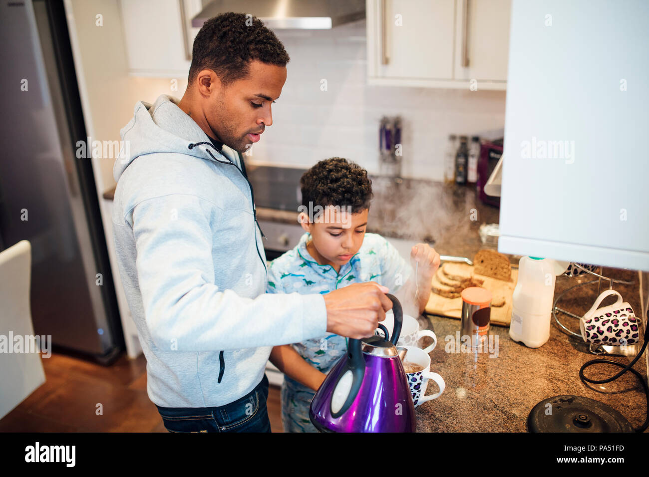 Little boy is helping his father while he makes tea in the morning ...