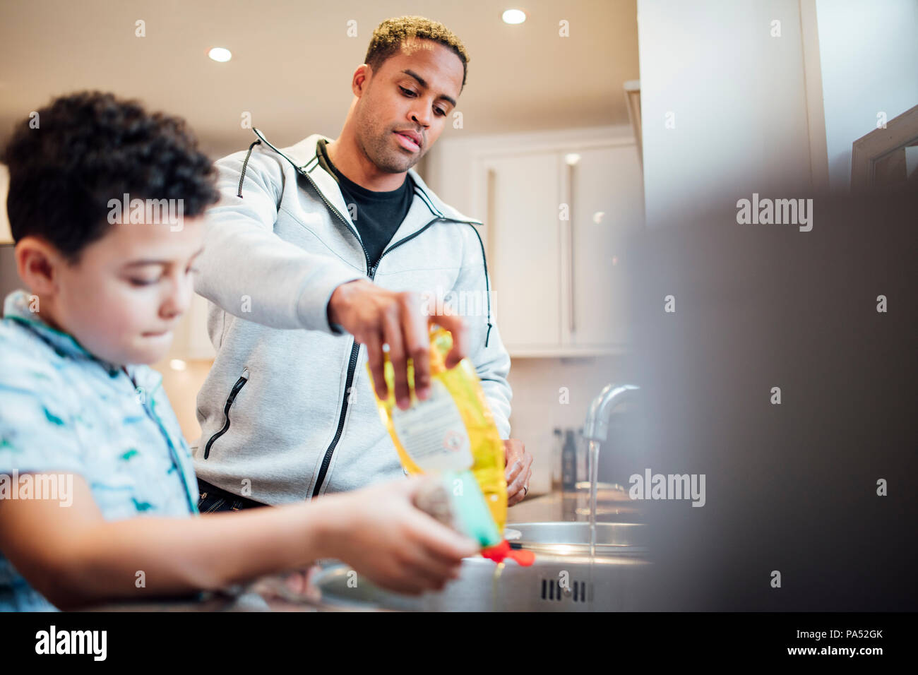 Little boy and his father are washing the dishes together at home. They ...
