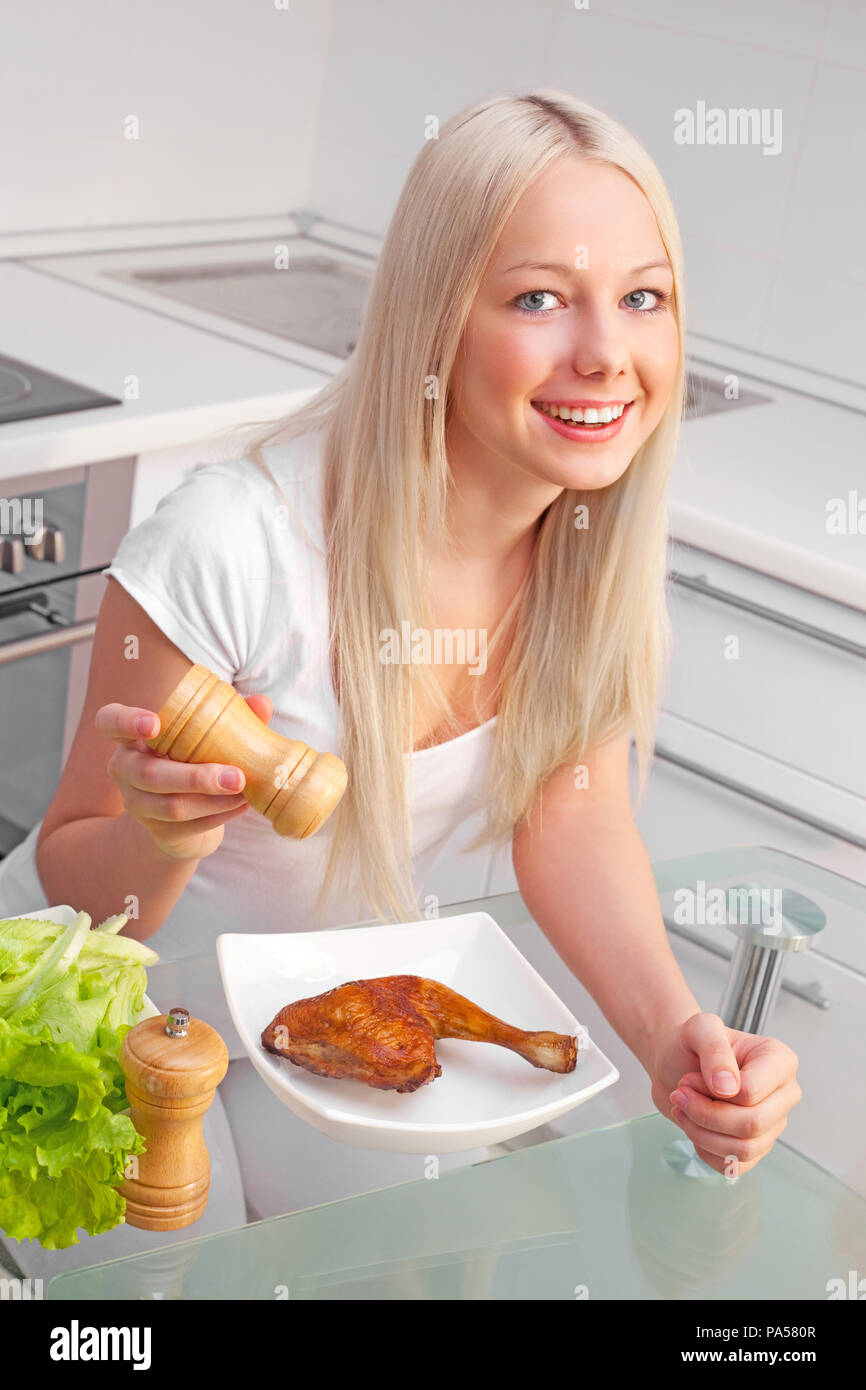beautiful young blond woman eating fried chicken at home in the kitchen ...