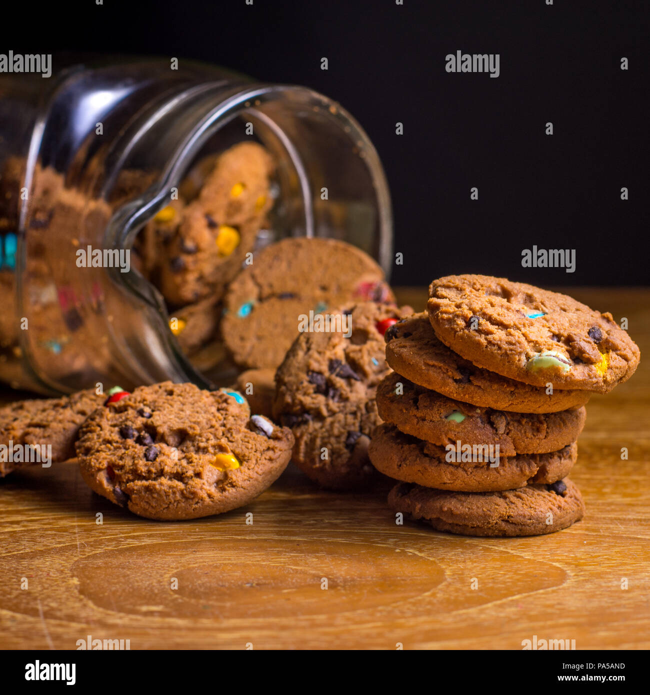 Choc chip smartie cookies falling out of jar on wooden table top Stock ...