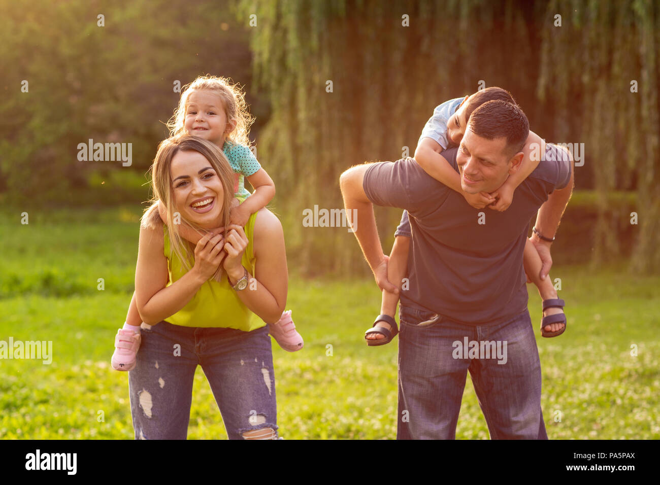 Happy family piggyback their children and have fun together in park ...
