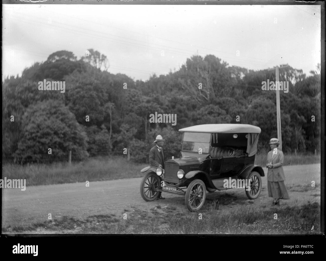 10 A man and woman standing beside a car on a road in a hilly, bushy ...