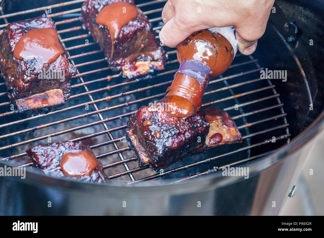 Cooking marinated beef short ribs on an outdoor barbecue and basting ...