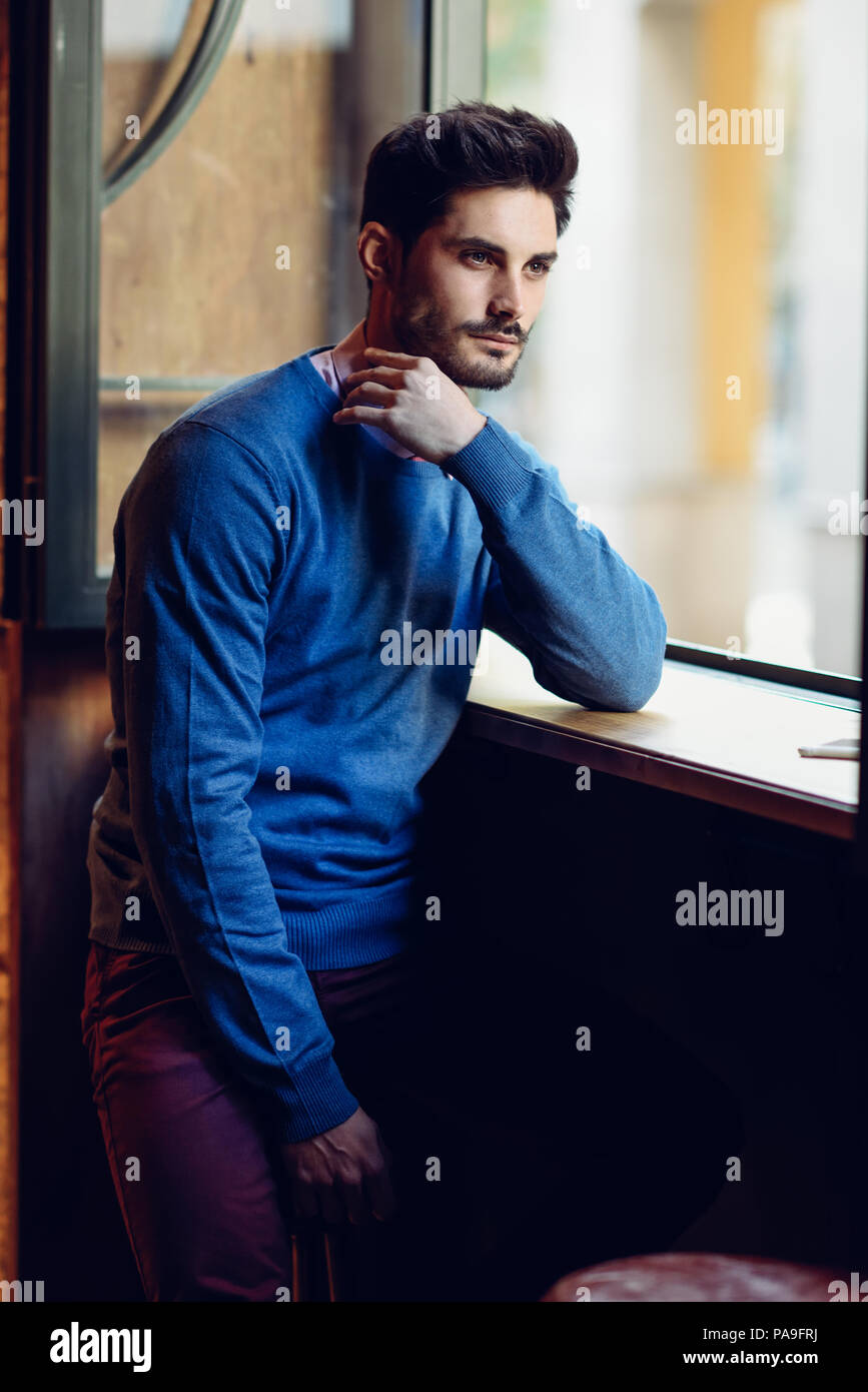 Thoughtful man with blue sweater with lost look near a window in a ...