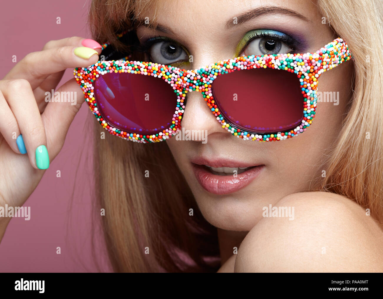 Young blonde serious woman with fun candy glasses on pink background ...