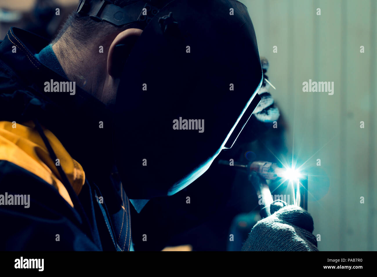 A welder welds a metal piece and sparks from welding fly in different ...