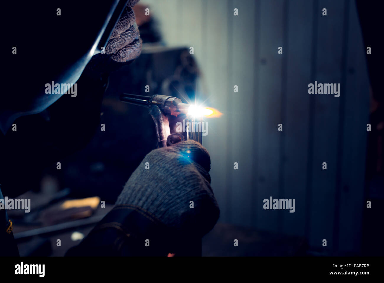 A welder welds a metal piece and sparks from welding fly in different ...