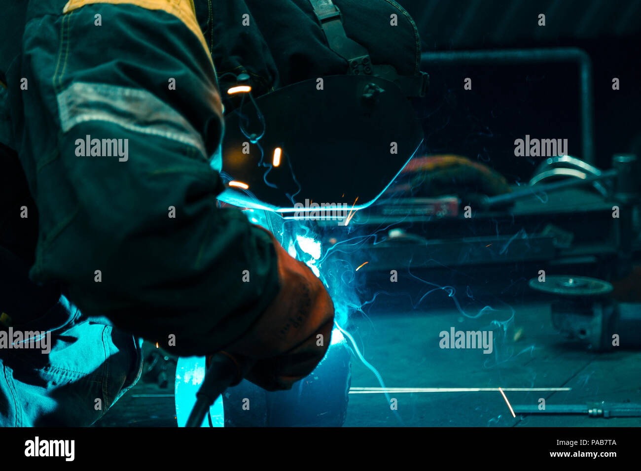 A welder welds a metal piece and sparks from welding fly in different ...