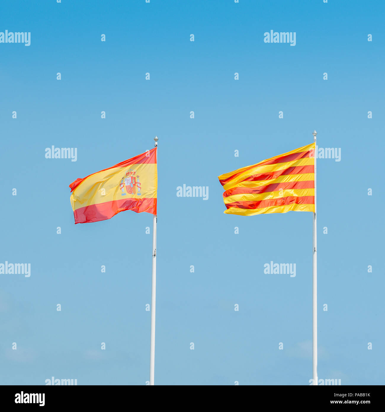 Catalonian and Spanish flags flying on a mast against a blue sky. The ...