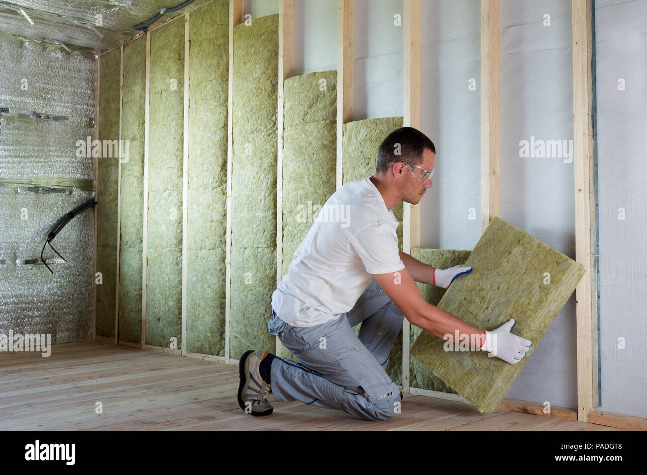 Worker in protective goggles and respirator insulating rock wool ...